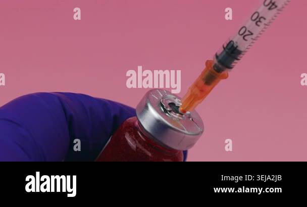 Syringe needle penetrating the rubber stopper of a medical vial held by ...