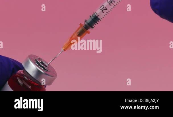 Hand holding a medical glass vial while a syringe needle inserts into ...