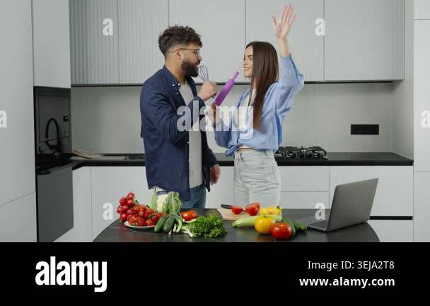 Joyful couple singing and dancing in the kitchen while cooking Stock ...