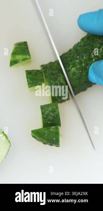 Fresh cucumber cutting close up on white kitchen board. Chef hands in ...
