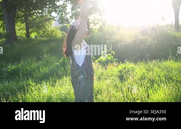 Cheerful young Asian woman dancing in green filed at golden sunset in ...