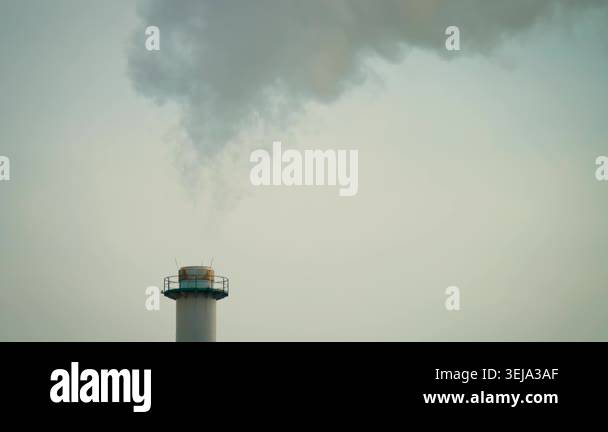 Factory chimney emitting heavy plume of smoke into cloudy atmosphere ...