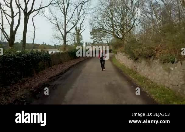 Wellness middle aged woman jogging along quiet lakeside pathway ...