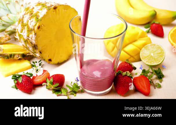 pink fruit smoothie in glass with straw surrounded by fresh pineapple ...