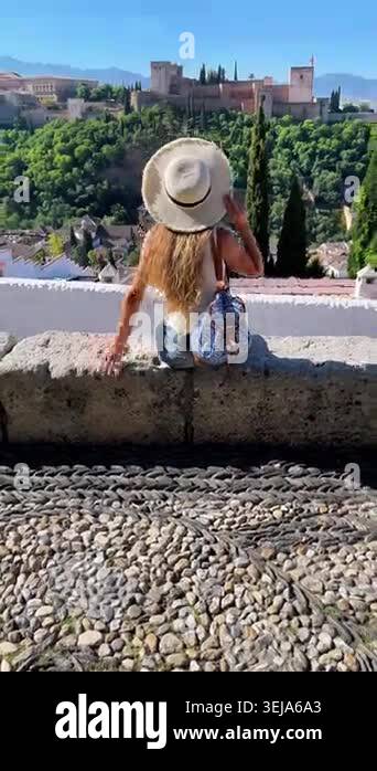 Tourist woman sitting on a wall looking at Alhambra palace in Granada ...