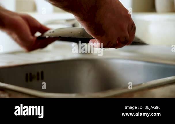 A person's hands are busy cleaning a dark, flat pan in a shiny ...