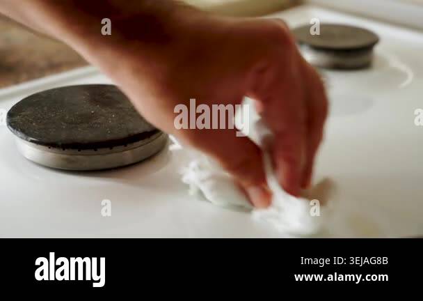 A person's hand cleaning a white gas stovetop burner with a cloth. The ...