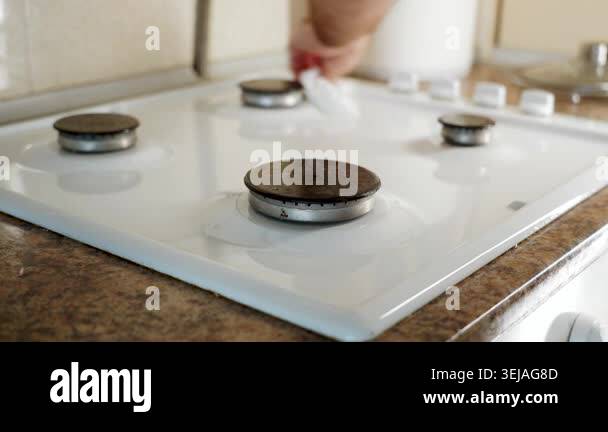 A man's hand uses a cloth to clean a dirty white gas stove top in a ...