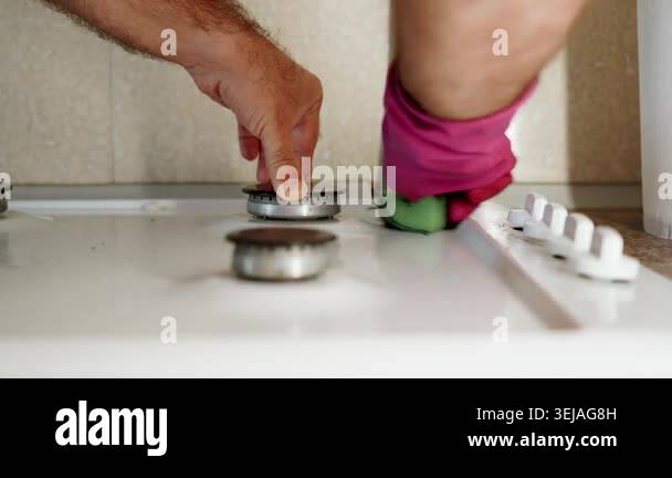 A person wearing a pink protective glove scrubs a dirty gas stovetop ...