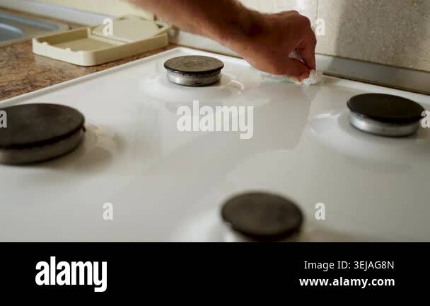 A man's hand wipes a white gas stove top with a soft cloth. The kitchen ...