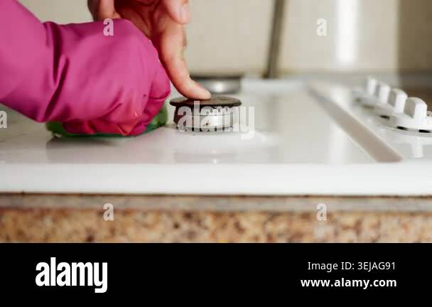 A person wearing a bright pink rubber glove scrubs a white gas stove ...