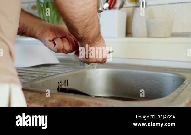 Man's hands cleaning a small sharp knife under a running faucet in a ...