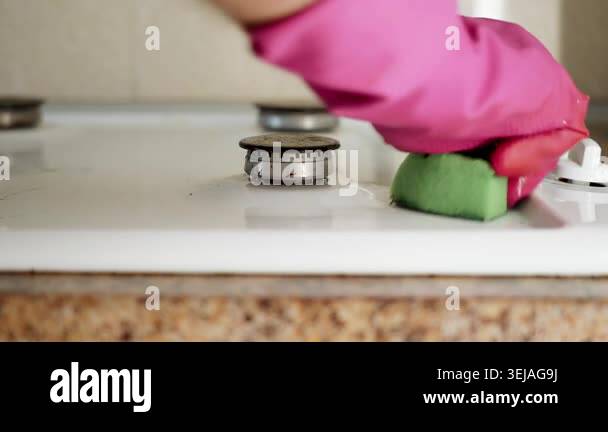 Close up of a person cleaning a white kitchen gas stove. A gloved hand ...