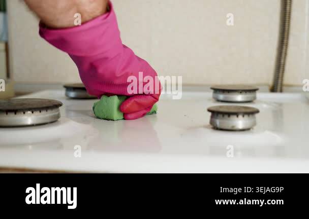 Close up of a person wearing a pink glove cleaning a gas stove burner ...