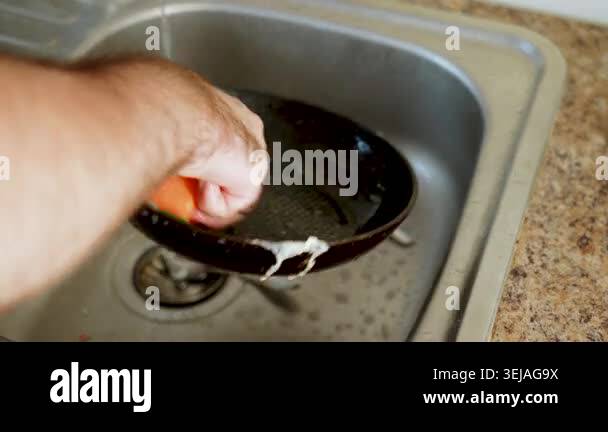 A person's hand washes a frying pan with water in a stainless steel ...