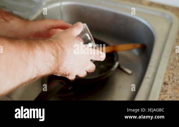 Hands clean a dirty frying pan, glass, and wooden spatula with an ...