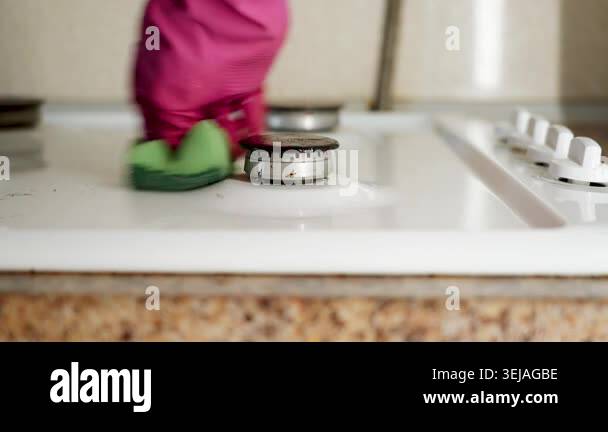 A person in a pink glove uses a green sponge to clean a dirty white gas ...