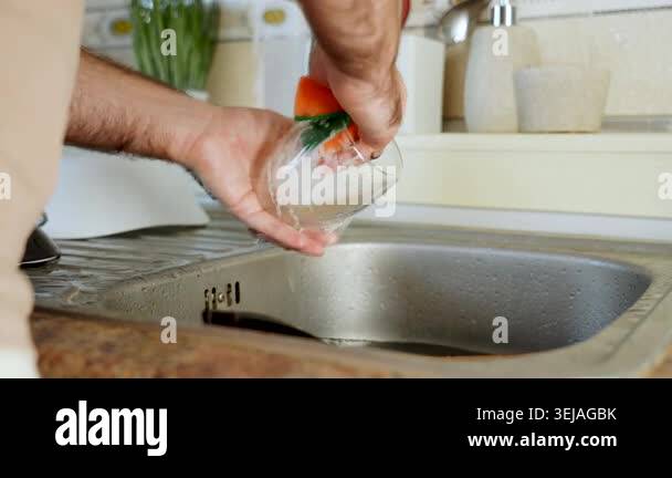 A man's hands scrub a clear drinking glass with a sponge and soap under ...