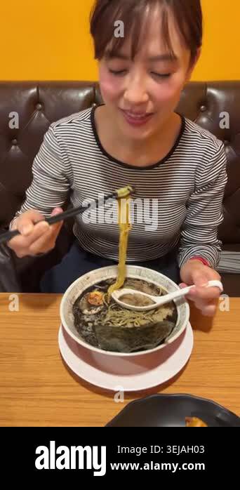 Hungry young Asian woman eating delicious hot dark broth noodle soup ...
