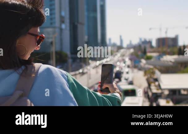 A young woman takes a photo of the Tel Aviv cityscape on her smartphone ...
