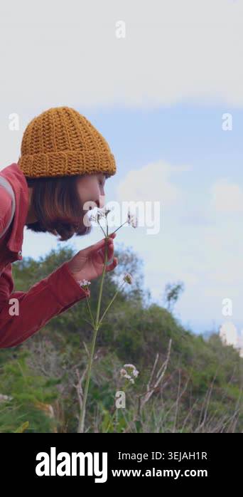 vertical shot. A girl sniffs a flower in a meadow, wearing a mustard ...