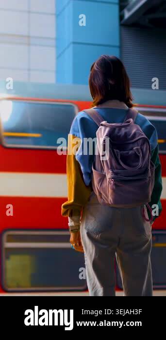 vertical shot. A girl with a backpack waits on a train platform, a city ...