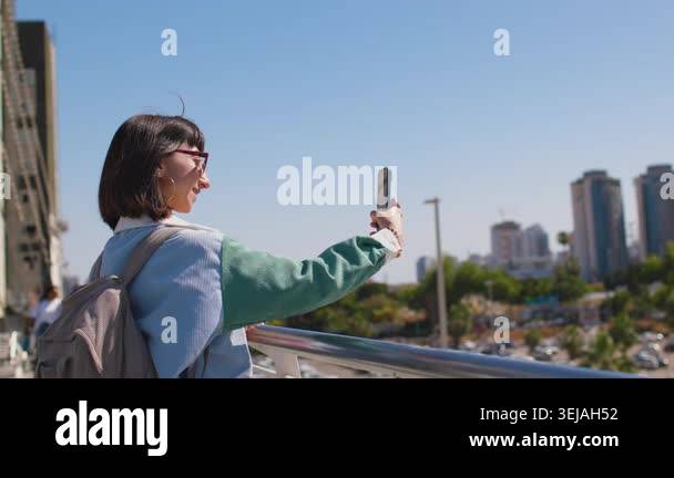 A young woman takes a photo of the Tel Aviv cityscape on her smartphone ...