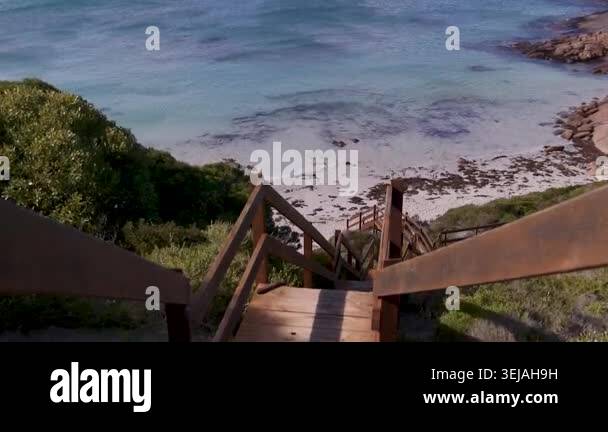 A wooden staircase descends to a remote beach with clear turquoise ...