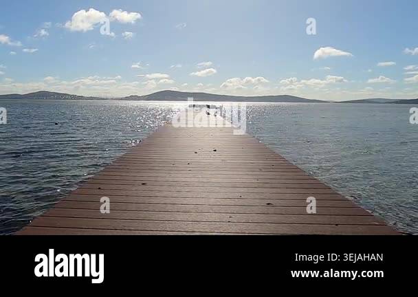 A wooden pier stretches into shimmering waters under a bright sky in ...
