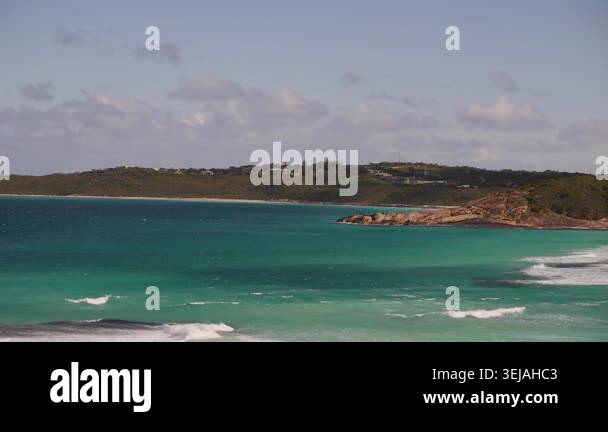 Waves gently lap against the rocky coastline under a partly cloudy sky ...