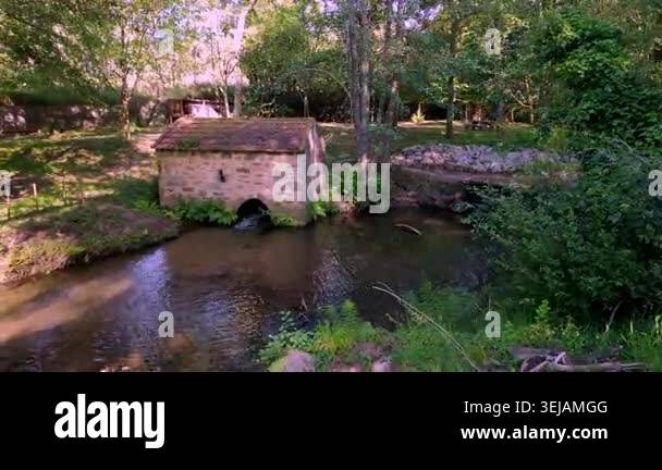 An ancient stone watermill stands peacefully beside a clear flowing ...