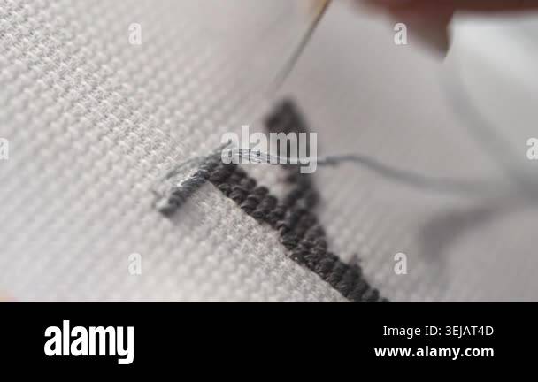 Intricate black thread forms precise cross stitch pattern on textured ...