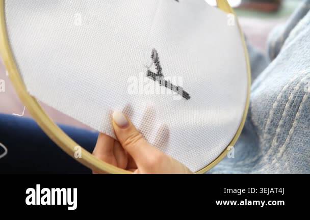 Close up of hands stitching black thread cross stitch on white fabric ...