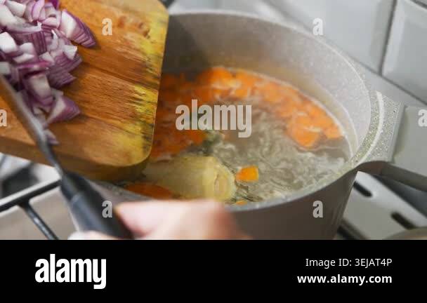 Chopped red onion pieces fall from wooden cutting board into simmering ...