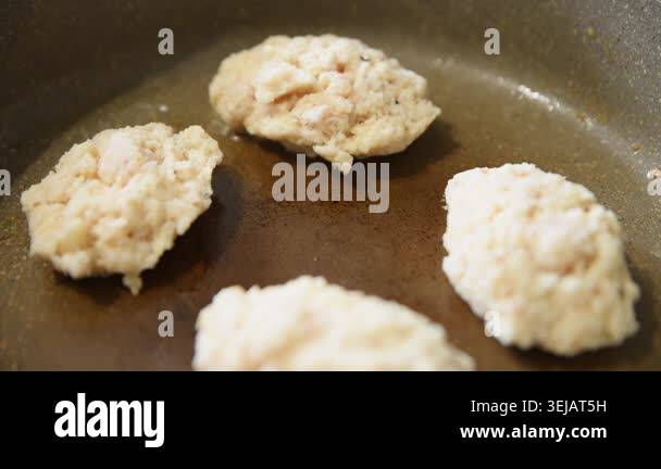 White fish patties lightly cooking in nonstick dark pan with golden ...