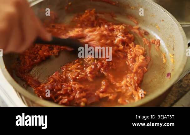 Hands stirring tomato paste combined with sauteed onions and grated ...