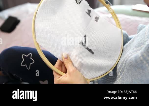 Person working on black cross stitch design on white fabric stretched ...