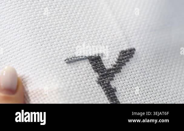 Hand securing precise stitches forming dark gray cross stitch letter y ...