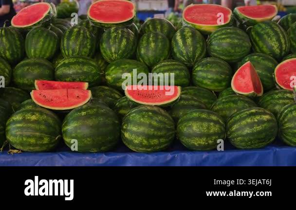 Row of stacked watermelons at market, ripe red slices displayed on blue ...