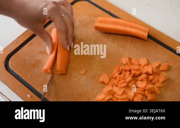 Woman carefully chopping fresh carrot into small cubes on wooden ...