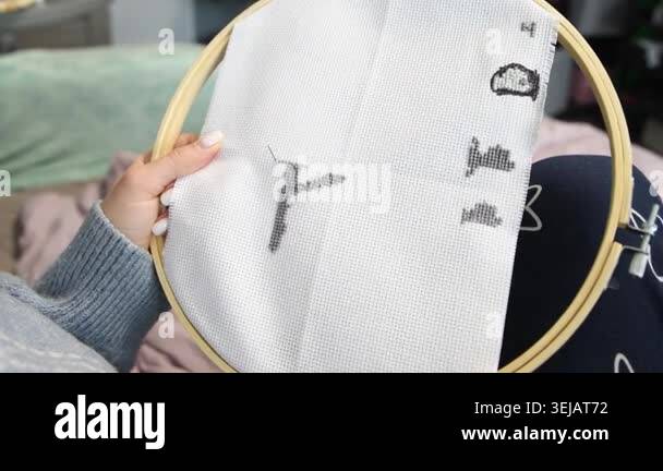 Close up of hand working black cross stitch letters on white fabric ...