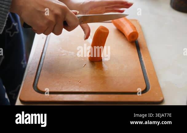 Person cutting peeled carrot into smaller chunks on brown chopping ...
