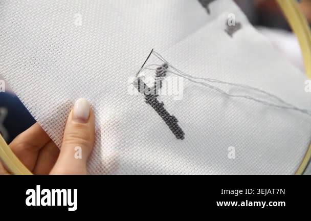 Close up view of hands creating black cross stitch design on white ...
