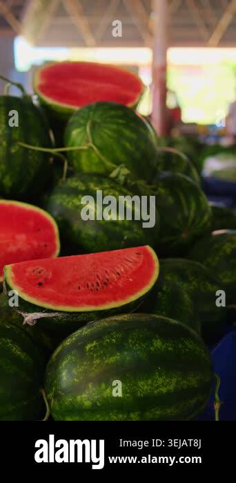 Row of stacked watermelons at market, ripe red slices displayed on blue ...