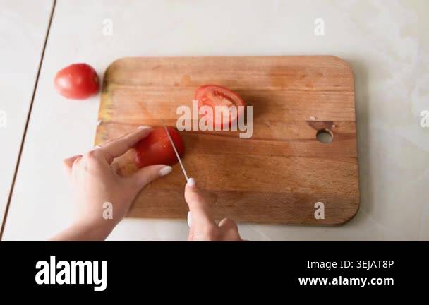 Person uses sharp knife to cut ripe red tomatoes into small pieces on ...