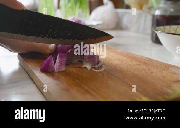 Hand slicing vibrant red onion with sharp black knife on wooden cutting ...