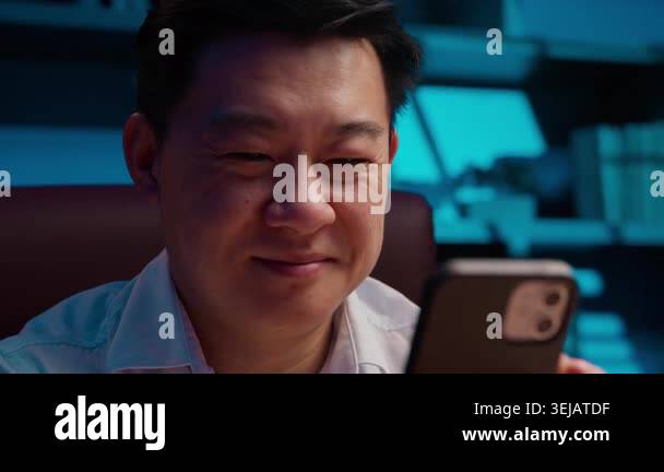 Laughing smiling Asian middle-aged business man scrolling mobile phone ...