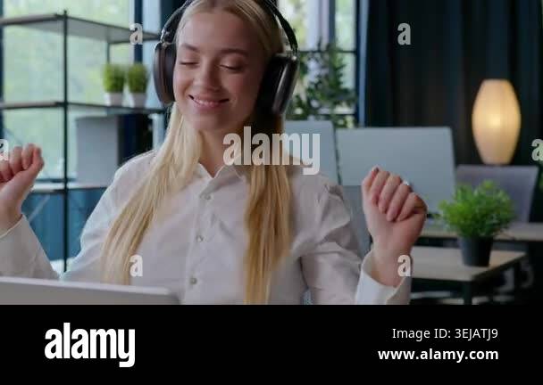 Happy Caucasian business woman in headphones listening music dancing ...