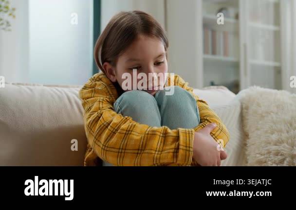 Depressed Caucasian little girl sad alone on couch at home hugging ...