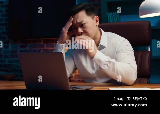 Fatigued unhappy Asian mature business man working laptop in evening ...